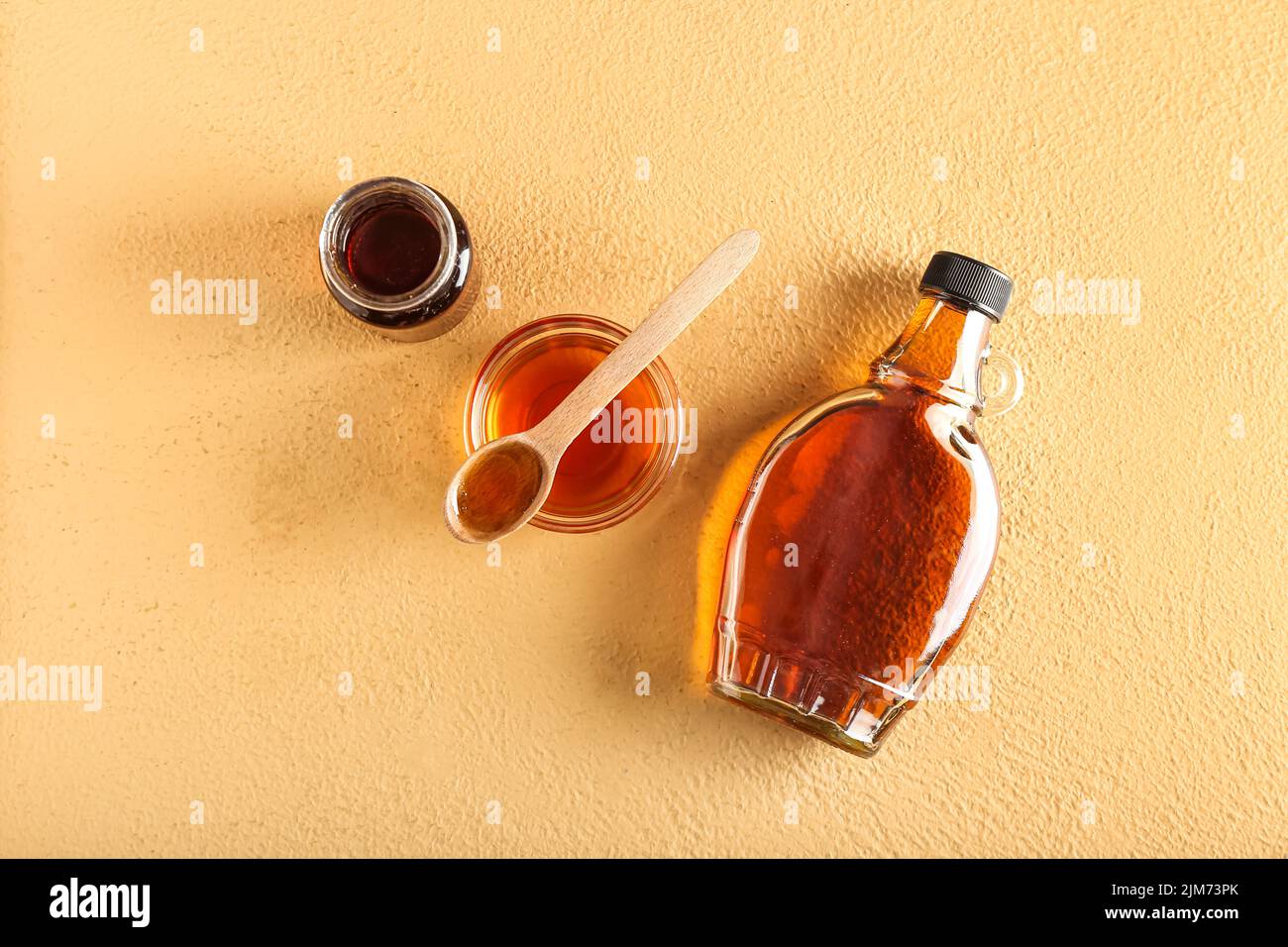 Bottles and bowl of maple syrup on color background Stock Photo - Alamy