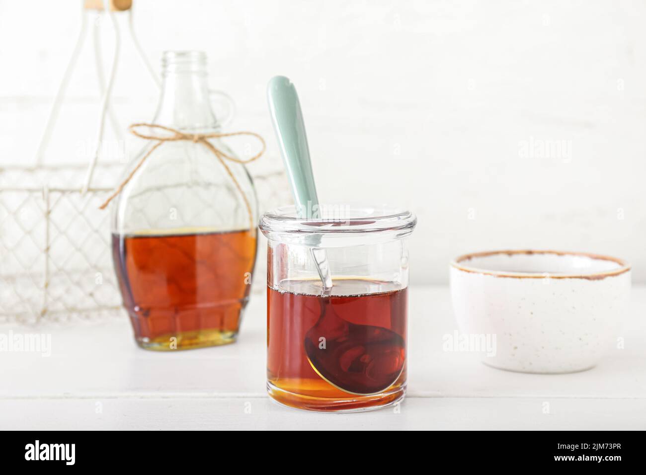 Glass jar of maple syrup and spoon on light background Stock Photo - Alamy