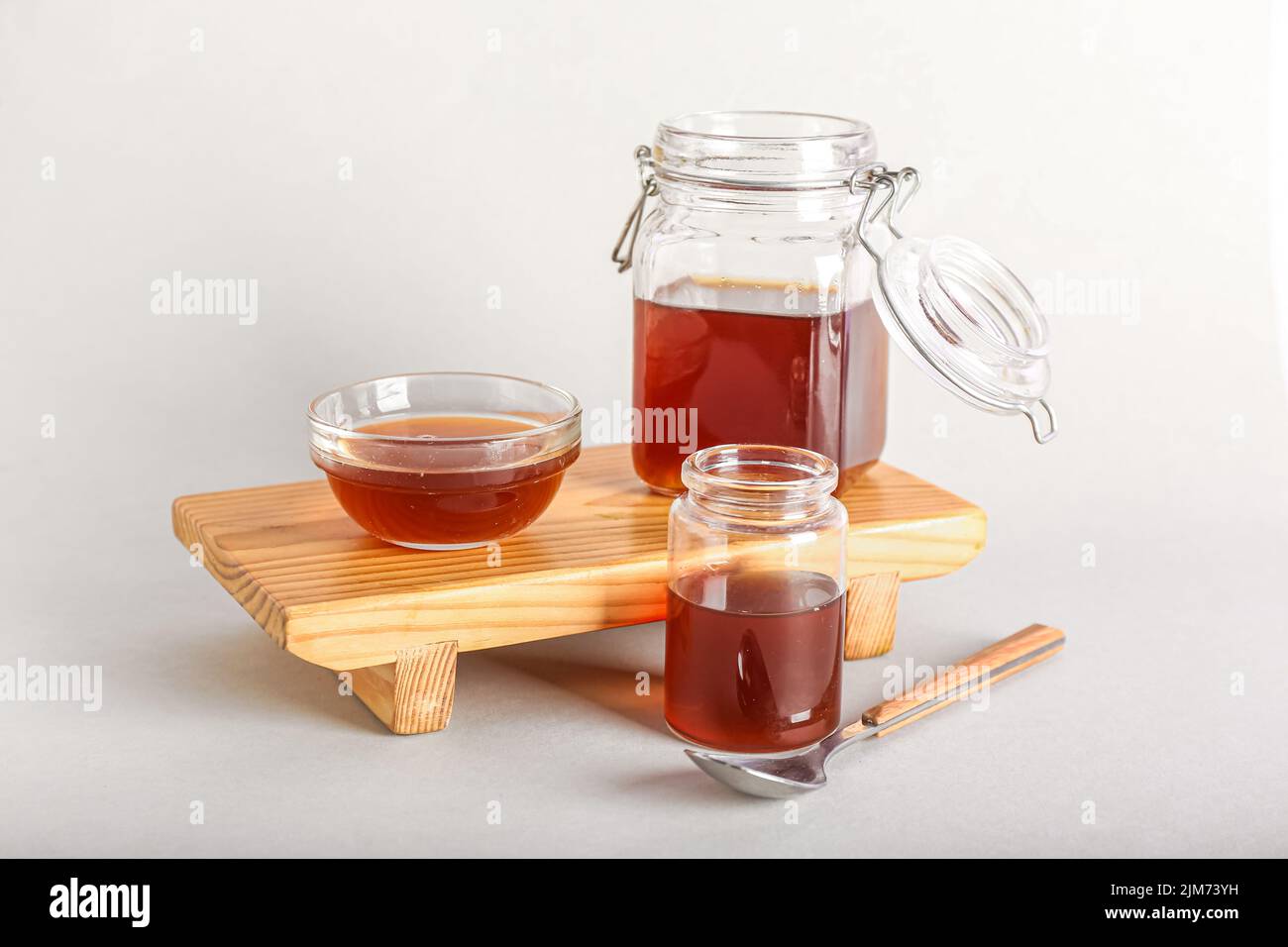 Wooden board with jars and bowl of tasty maple syrup on white ...