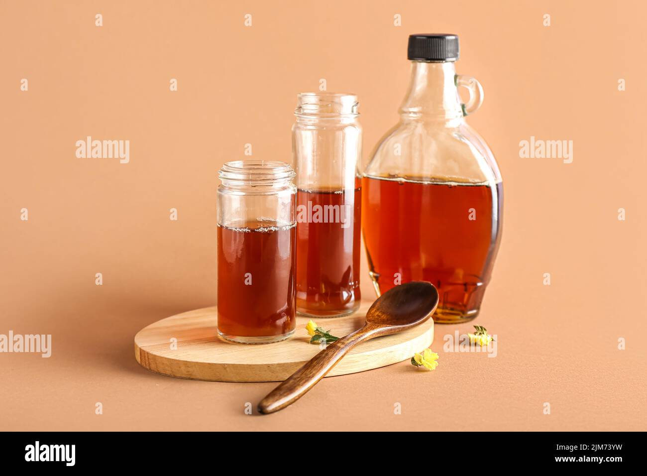 Wooden board with jars and bottle of tasty maple syrup on color ...