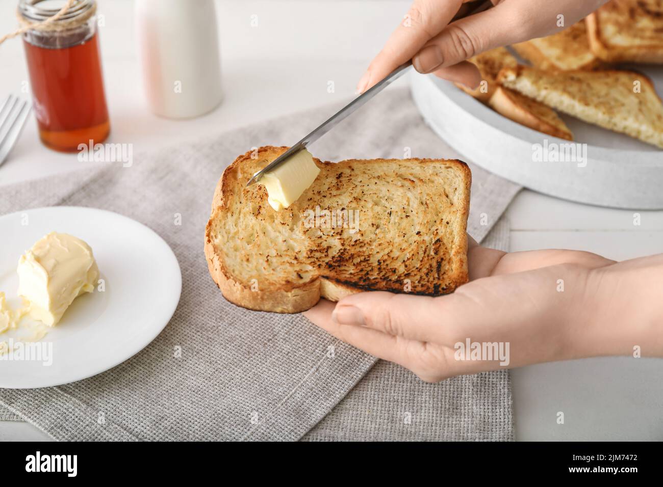 Woman spreading butter onto slice of roasted bread on table, closeup ...