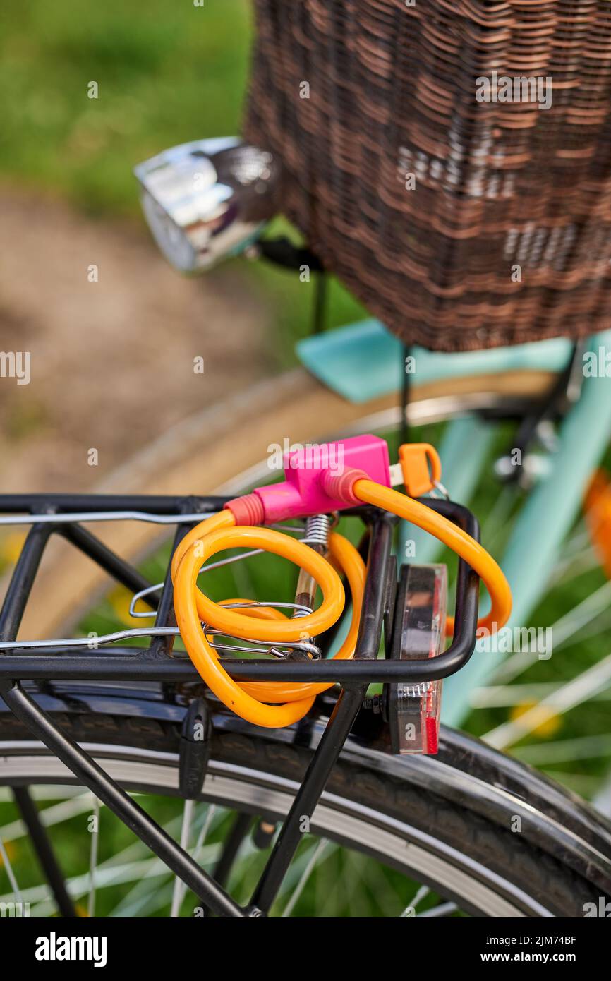 A vertical closeup of the back of a bike with an orange steel wire lock ...