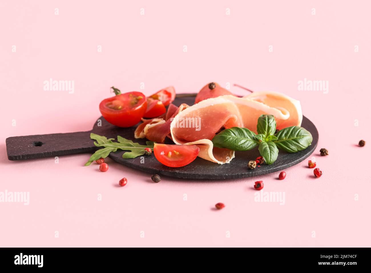 Slate board with delicious jamon, spices and tomatoes on pink ...