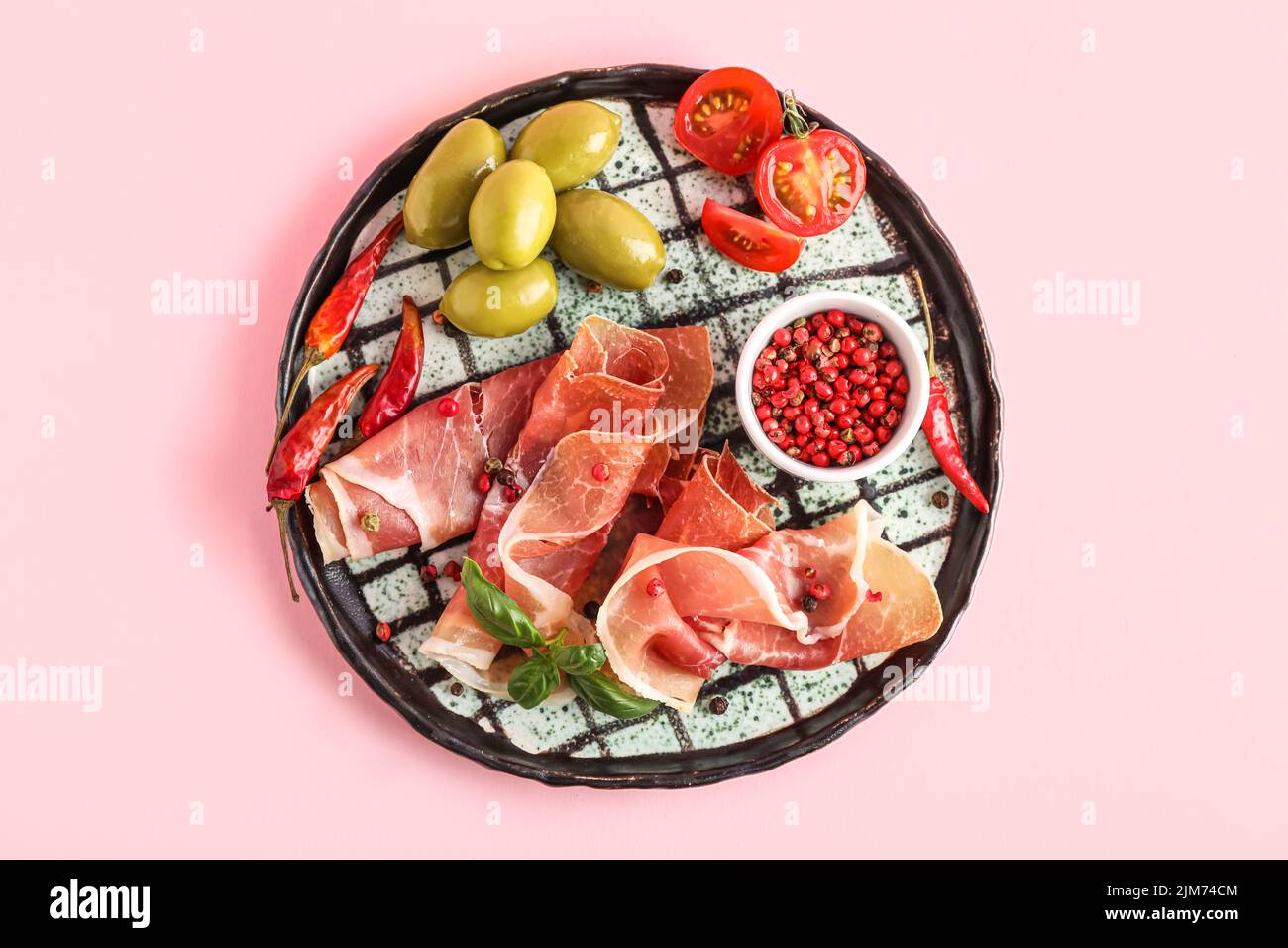 Plate with delicious jamon, olives, tomatoes and peppercorns on pink ...