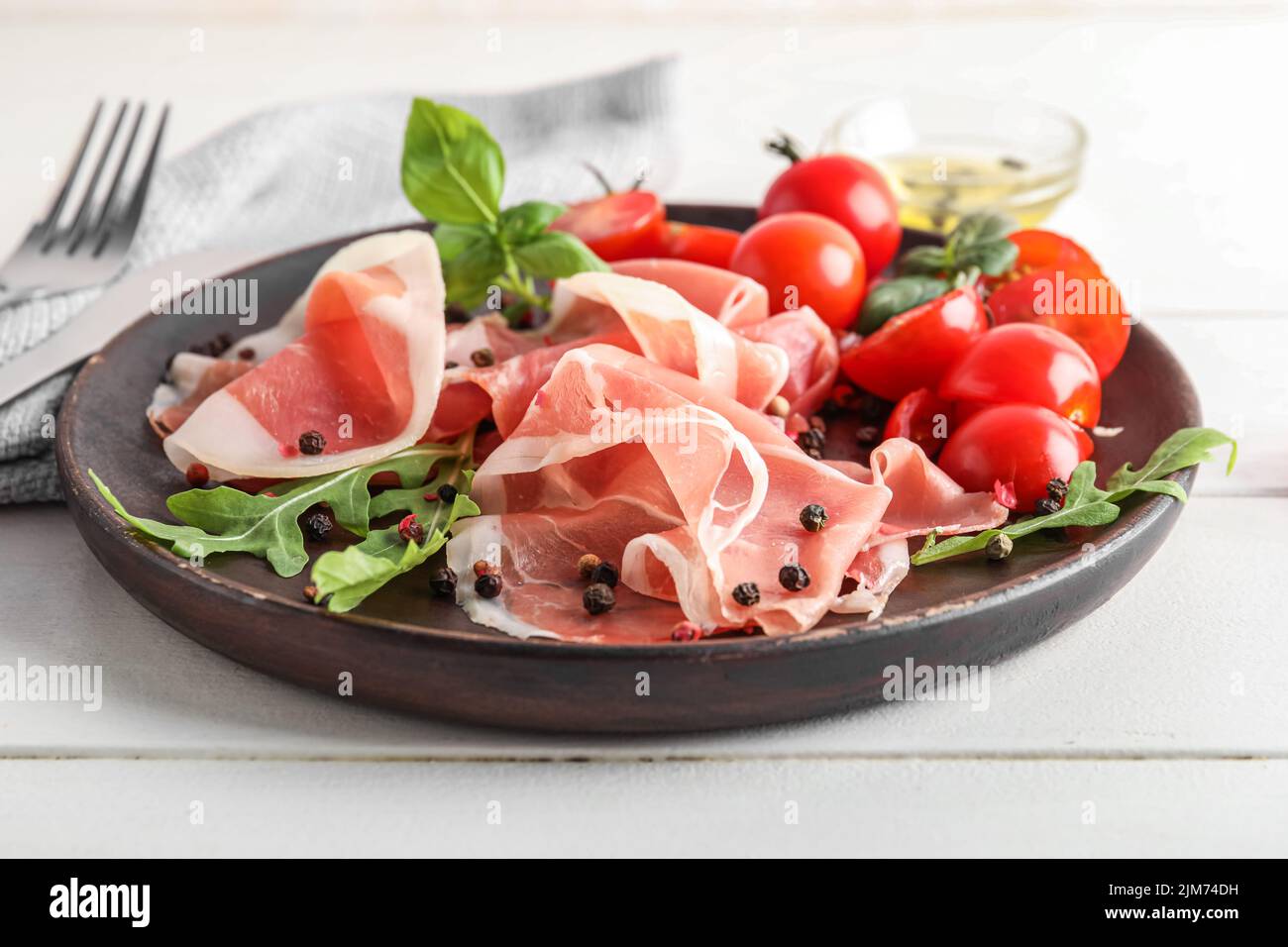 Plate with delicious jamon and tomatoes on light wooden background ...