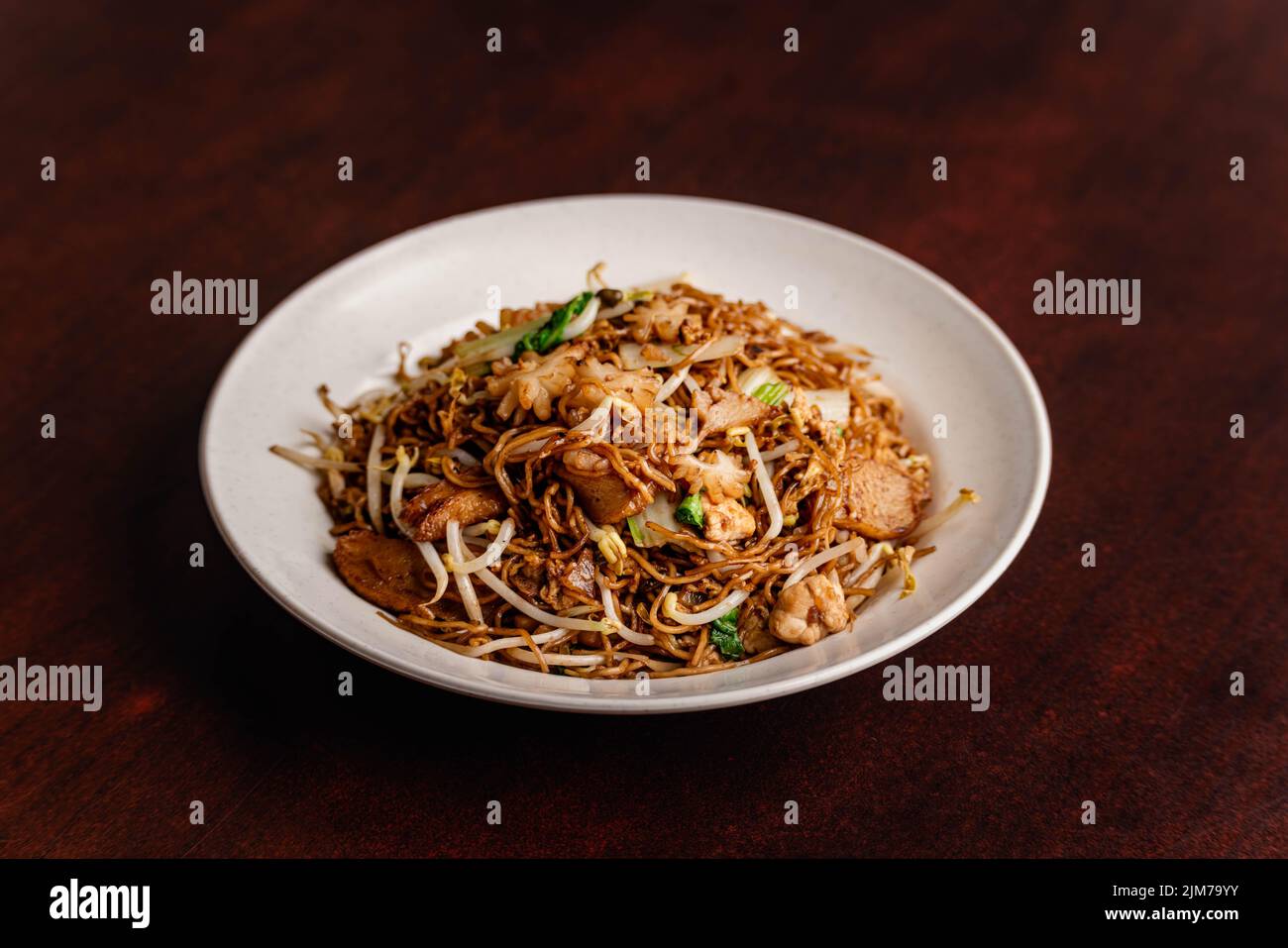 A closeup shot of a stir fried noodles in a white plate on a wooden ...