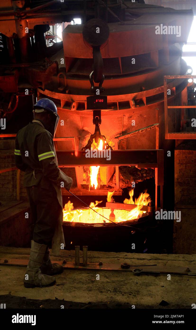A vertical wide shot of a worker watching hot molten forged steel rods ...