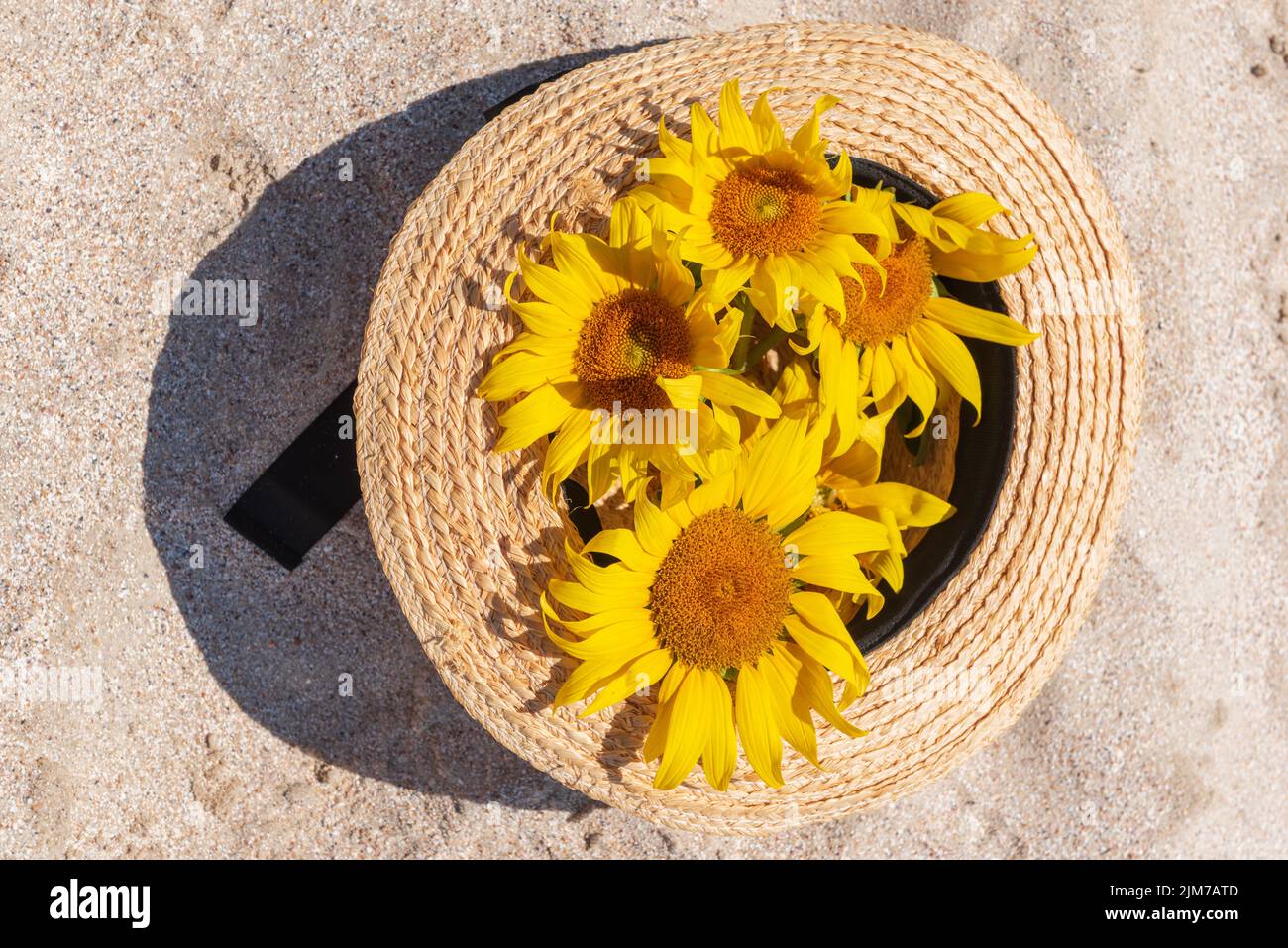 Top view of a straw hat filled with sunflowers, lying on the sea sand ...