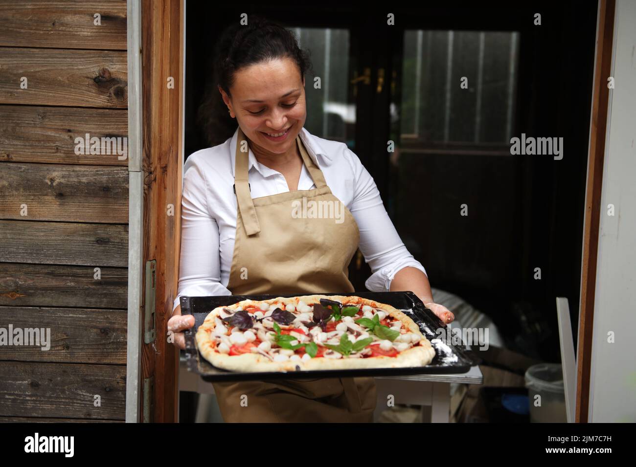 Middle-aged multiethnic woman, housewife holding a baking sheet with ...