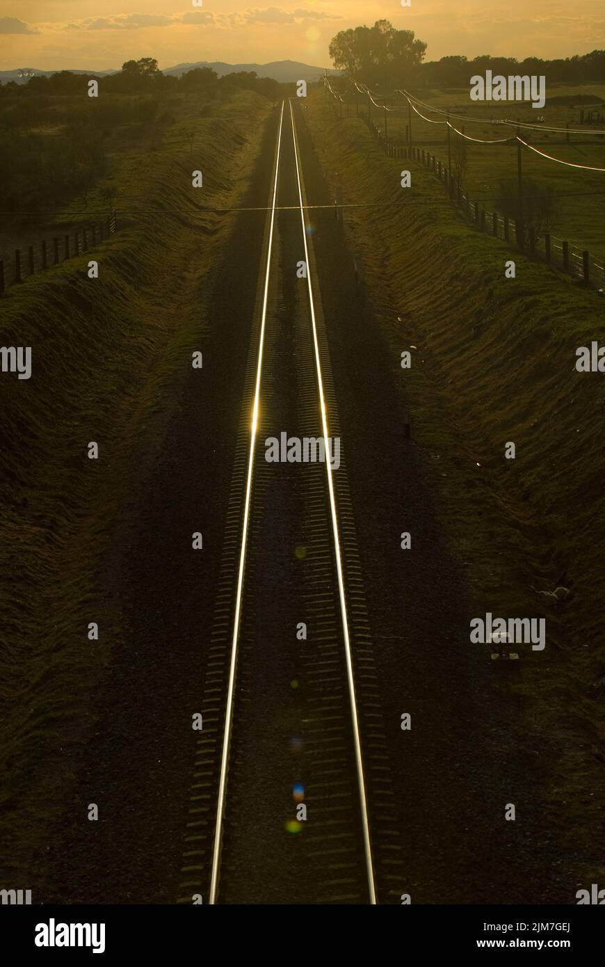 A vertical shot of a railway reaching the horizon and the setting sun ...