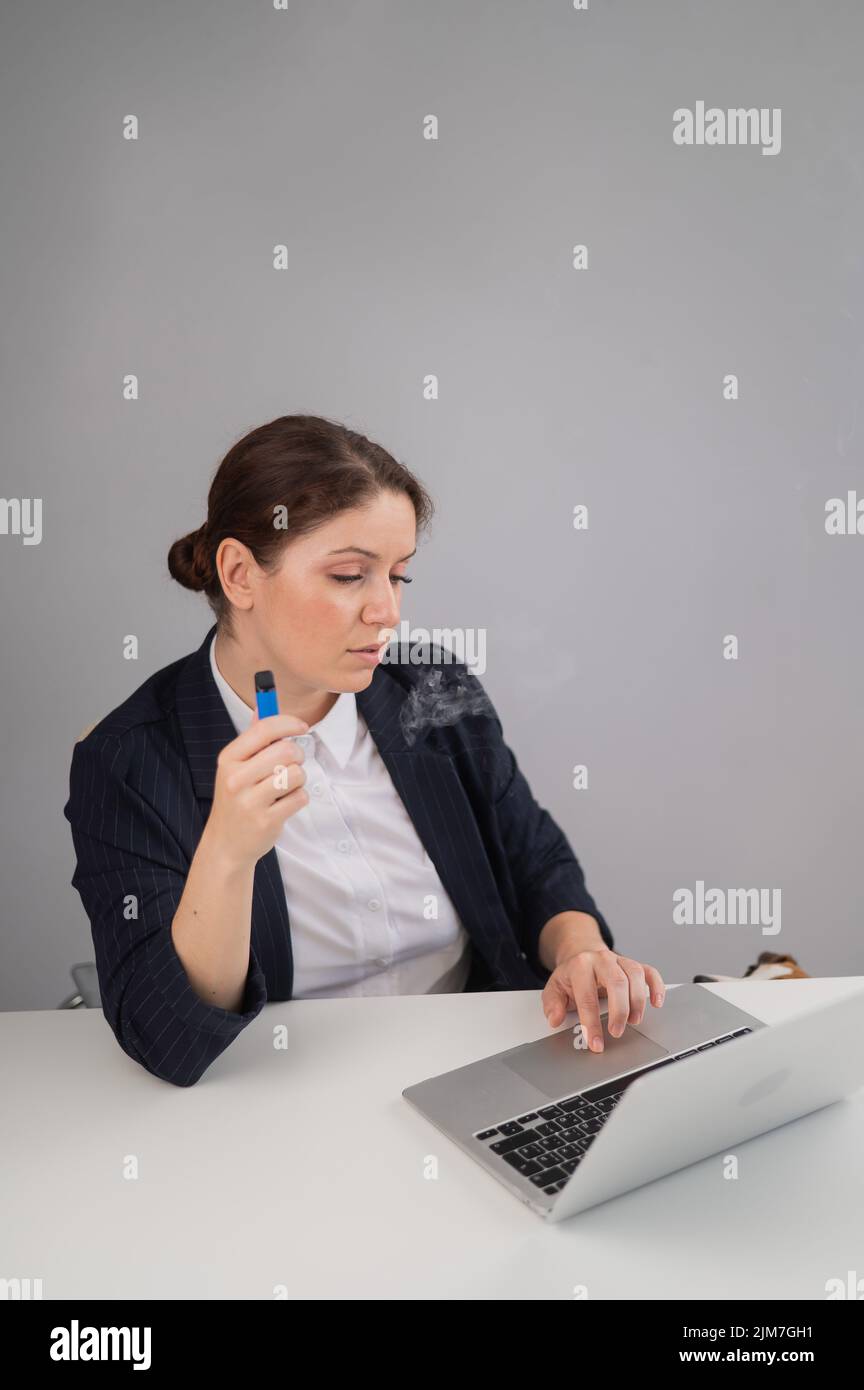 Business woman smoking a disposable vape while sitting at her desk ...
