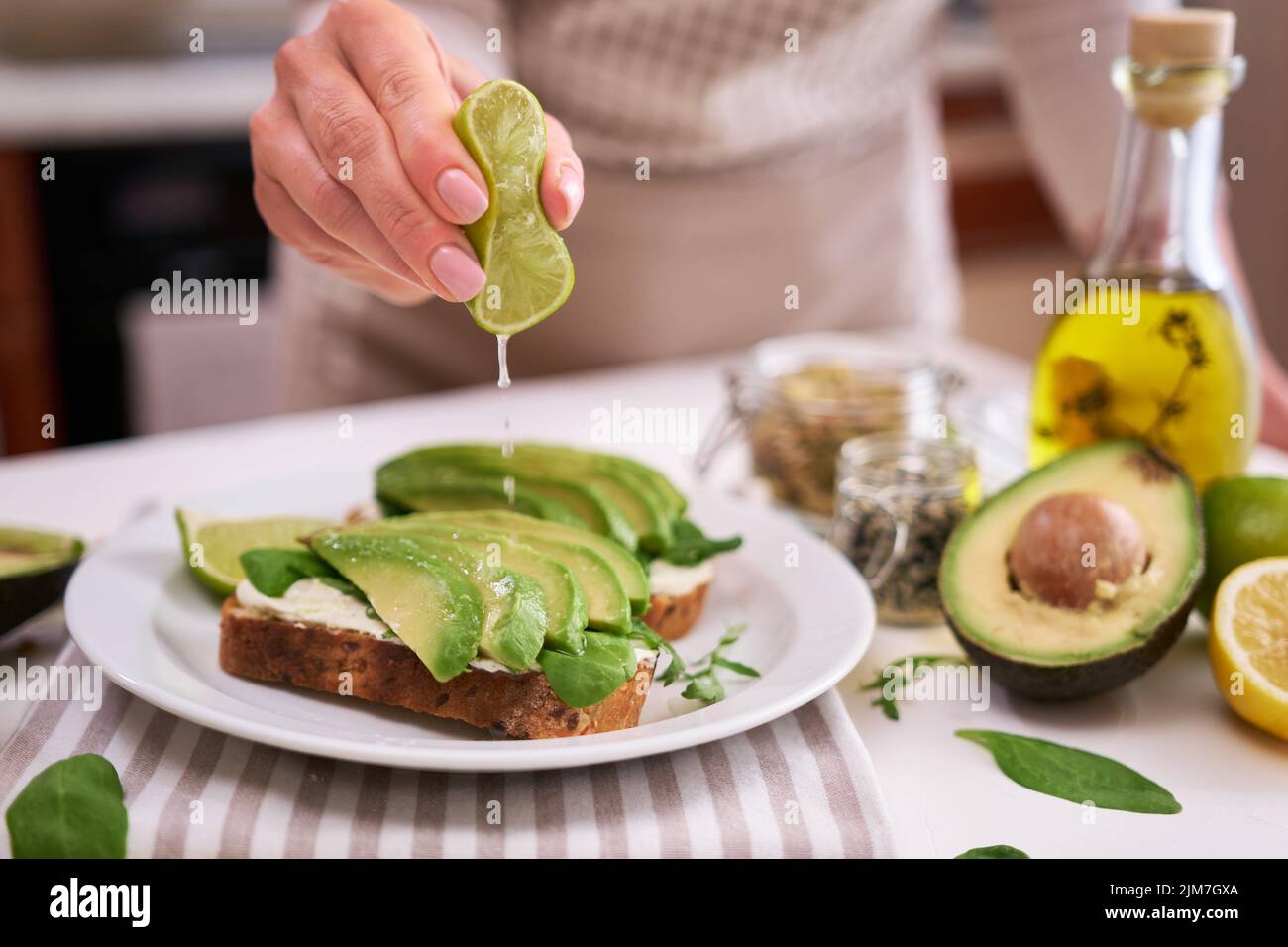 Woman squeezing fresh lime juice on a Avocado and cream cheese toasts ...