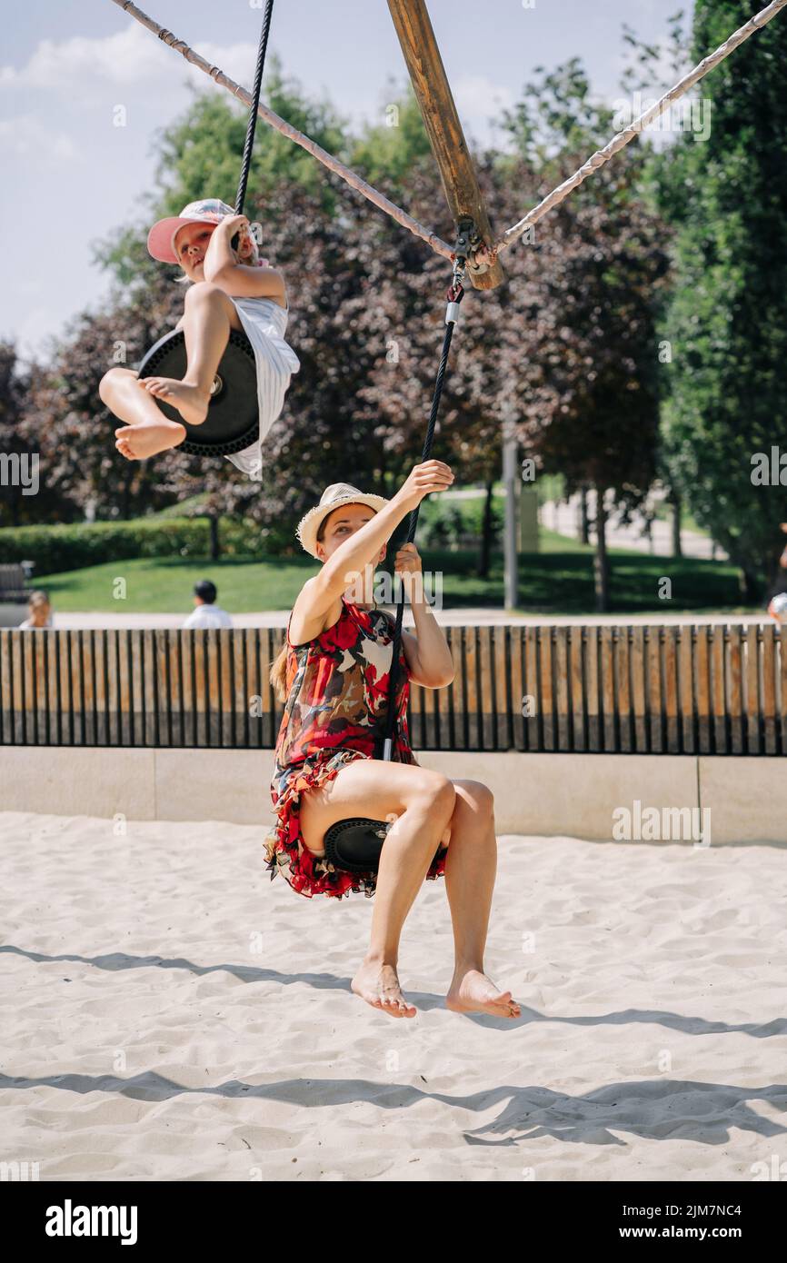 Mother and daughter in a swing having fun at the park playground. Mom and toddler swinging on ...