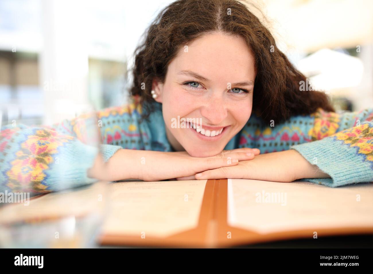 Front view portrait of a happy woman looking at you over a menu card in ...