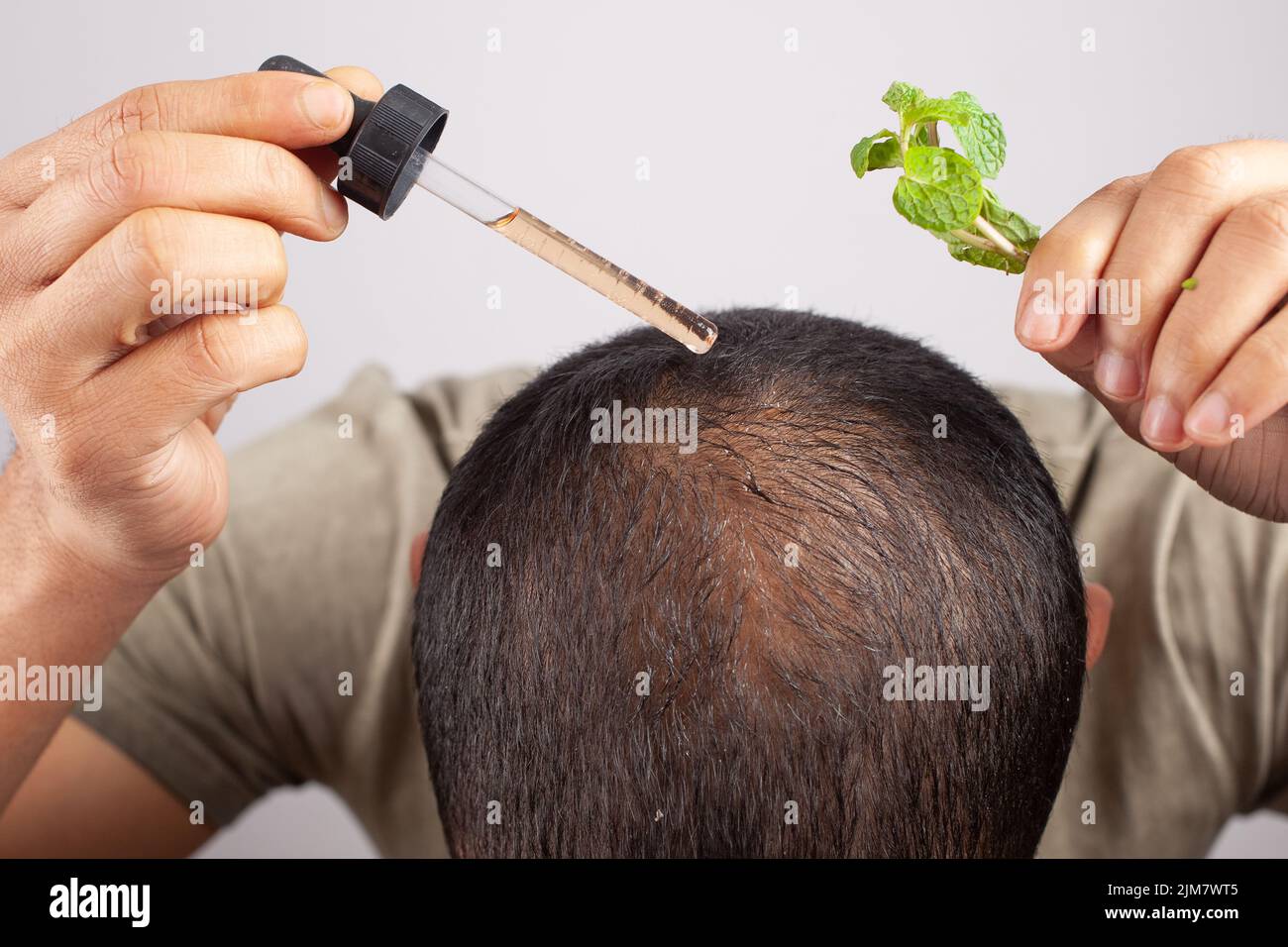 Indian guy using hair essential oil by a dropper on the top of scalp ...