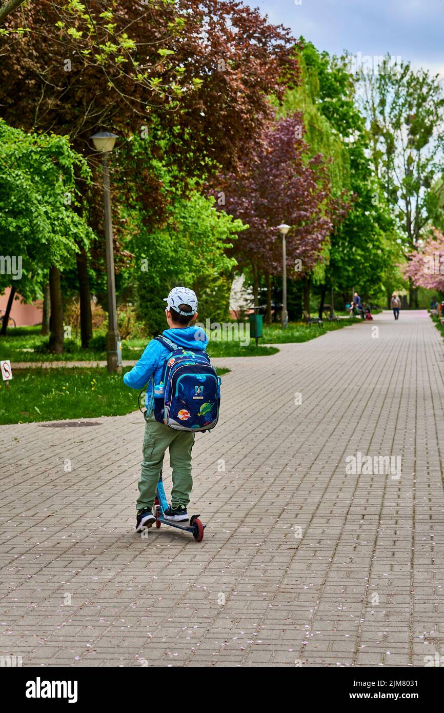 A boy with school backpack riding a scooter on a footpath in Rataje ...