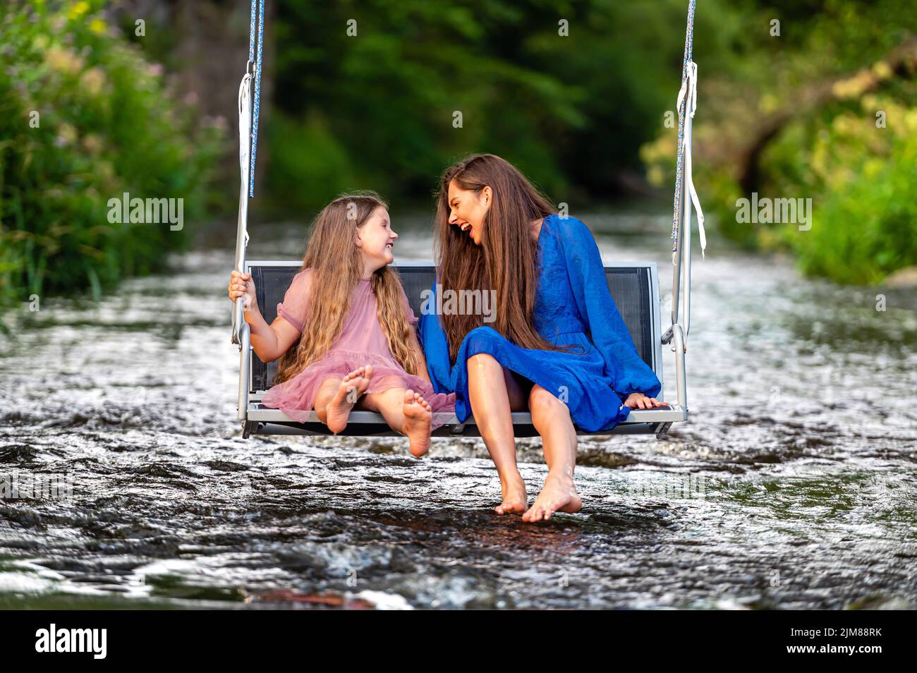 laughing woman and a young girl swing over a fast-flowing river ...