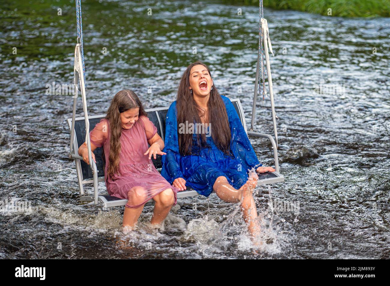laughing woman and a young girl swing over a fast-flowing river ...