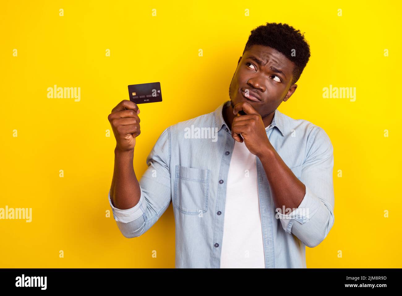 Photo of serious young brunet guy hold card look up wear jeans shirt ...