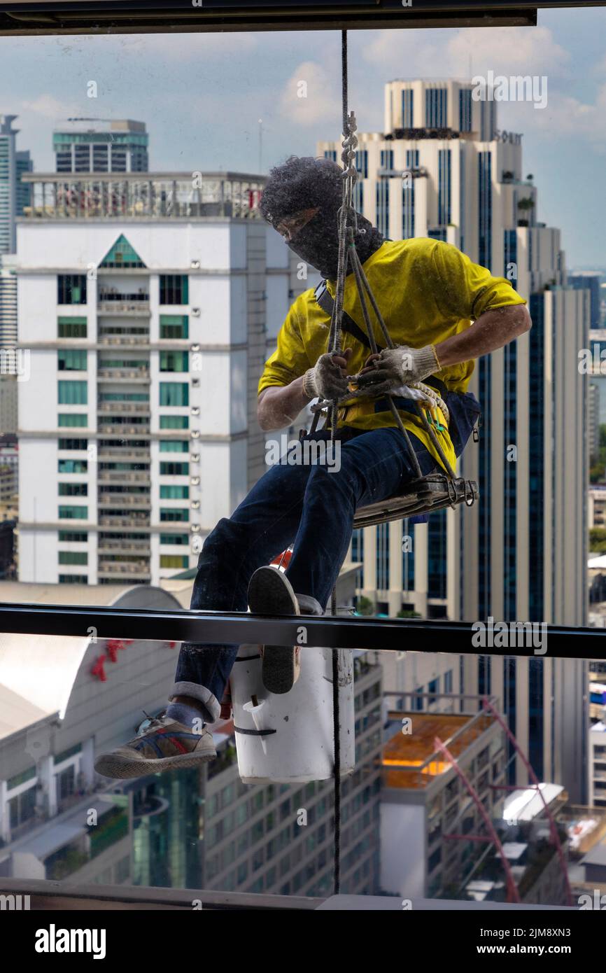 Thai workman repairing window in high rise building using rope and ...