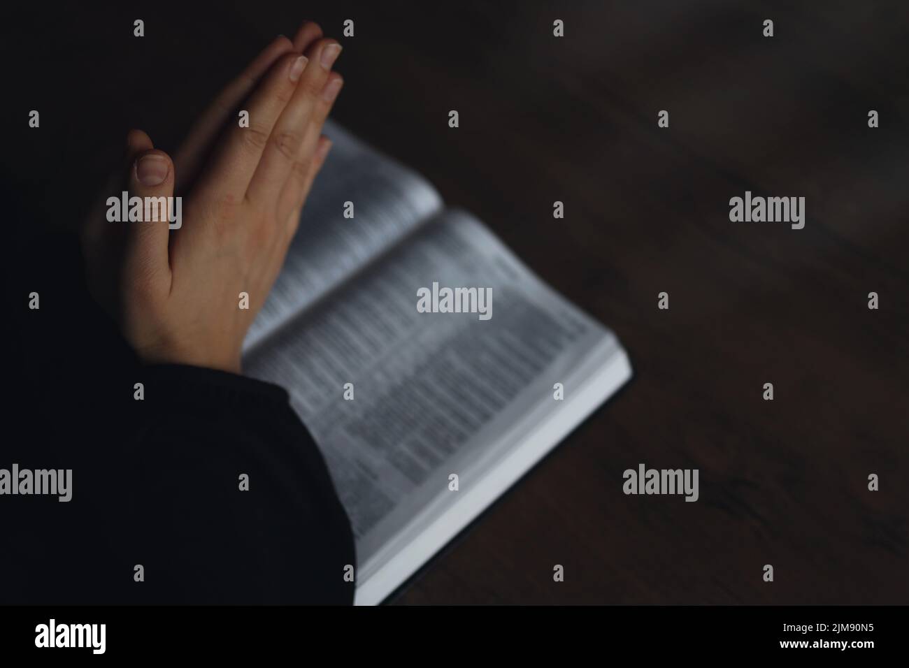 Woman hands on Bible. she is reading and praying over bible in a dark ...