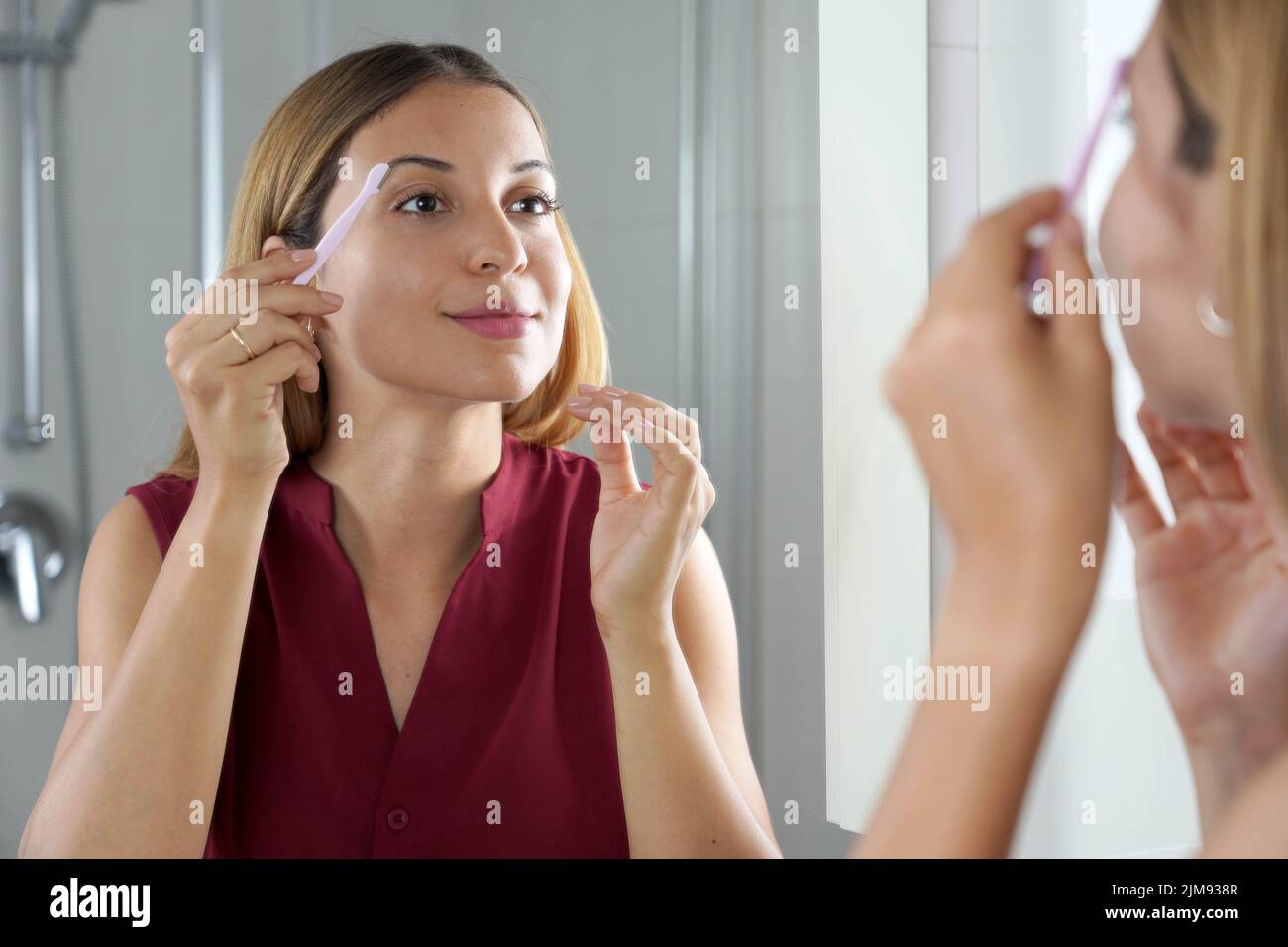 Close up of latin woman shaving her eyebrows with razor in the mirror ...
