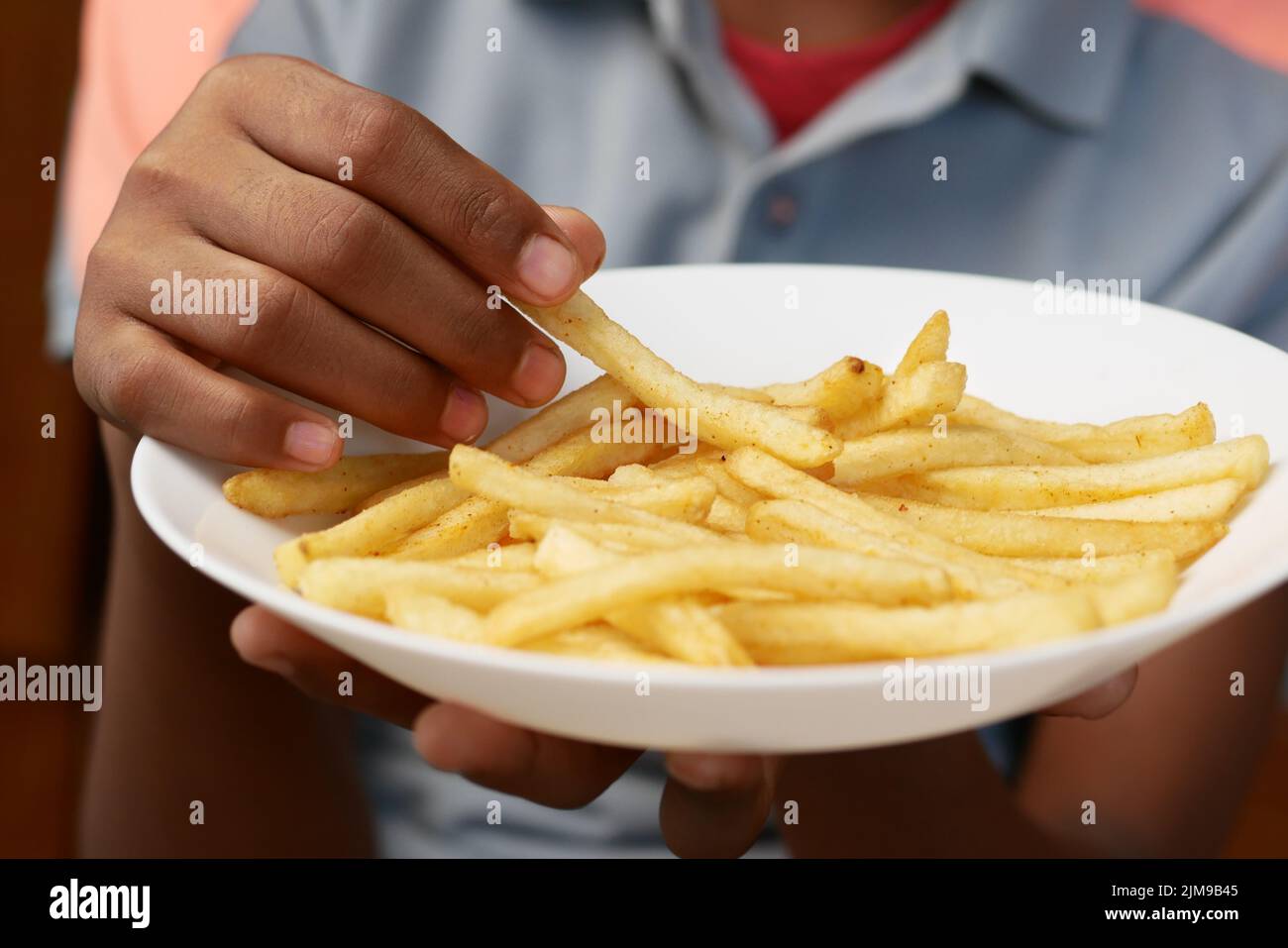 a teenage boy eating french fries while sited Stock Photo - Alamy