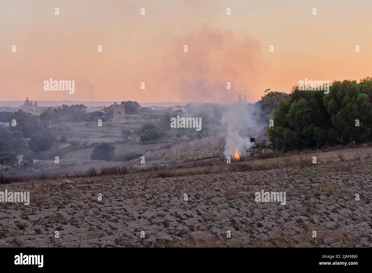Farmland landscape with glowing burn fire near dry forest. High risk of ...
