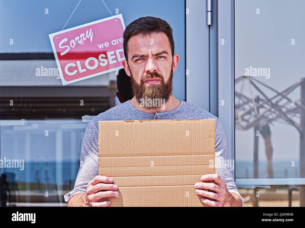 Unemployed guy with empty signboad near closed door office or cafe ...