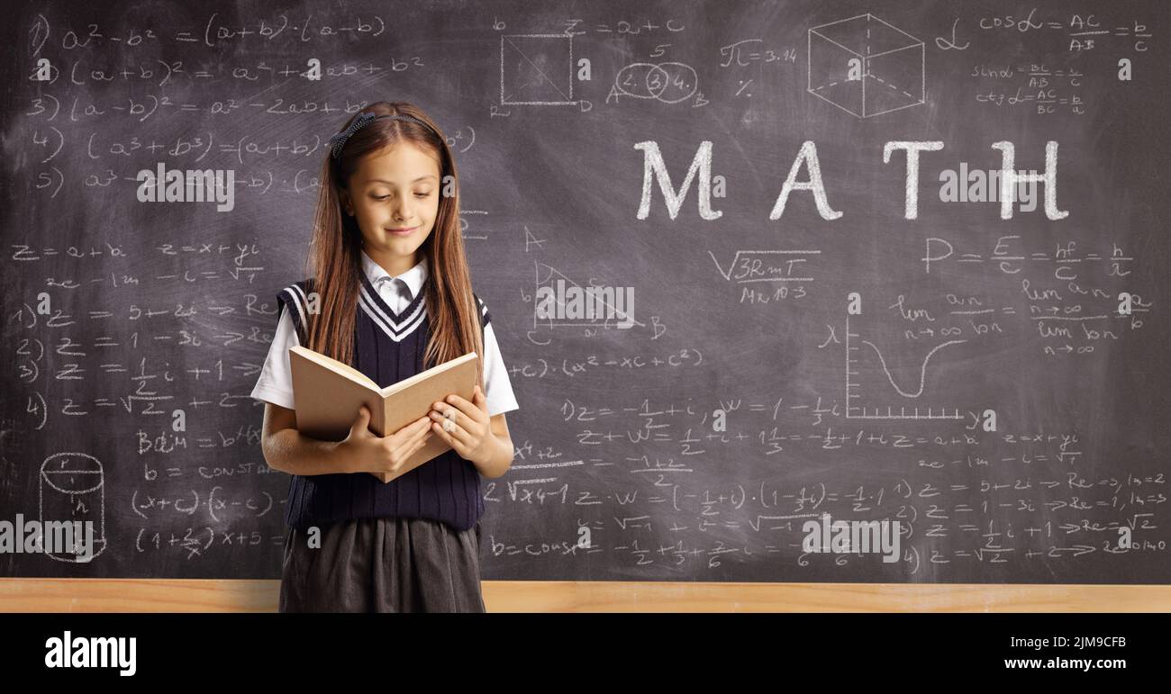 Schoolgirl reading a book and standing in front of a blackboard with ...
