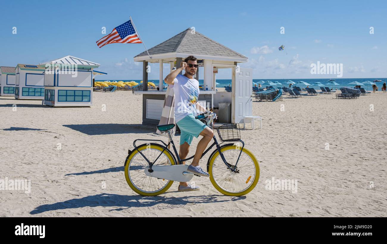Young men in a swim short on the beach Miami with a bicycle, colorful ...