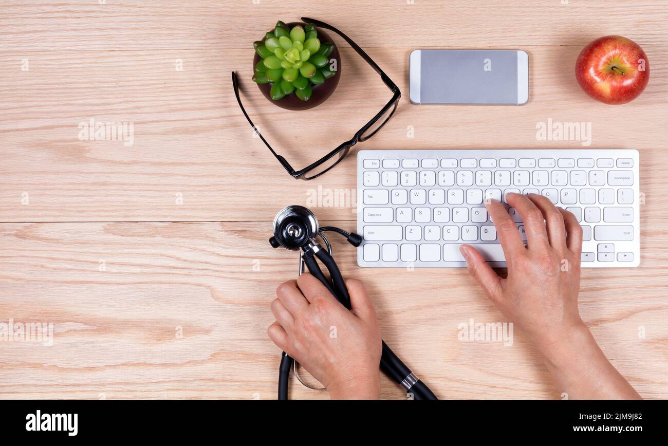 Hands picking up stethoscope while using computer keyboard on wooden ...