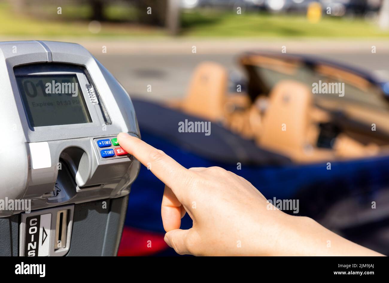 Hand selecting time on parking meter with convertible car in background ...