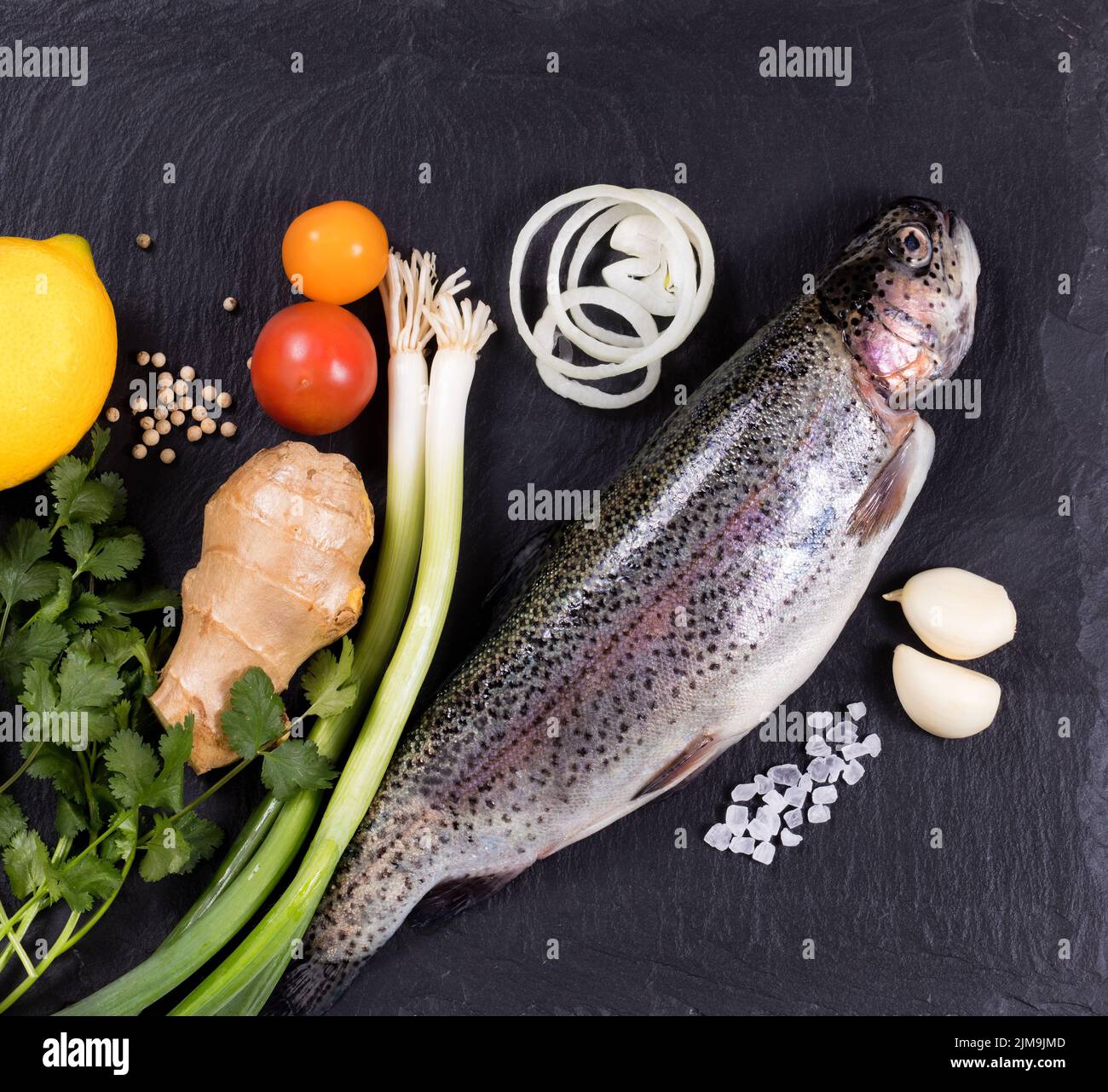 Fresh whole raw fish and herbs displayed on natural slate stone ...