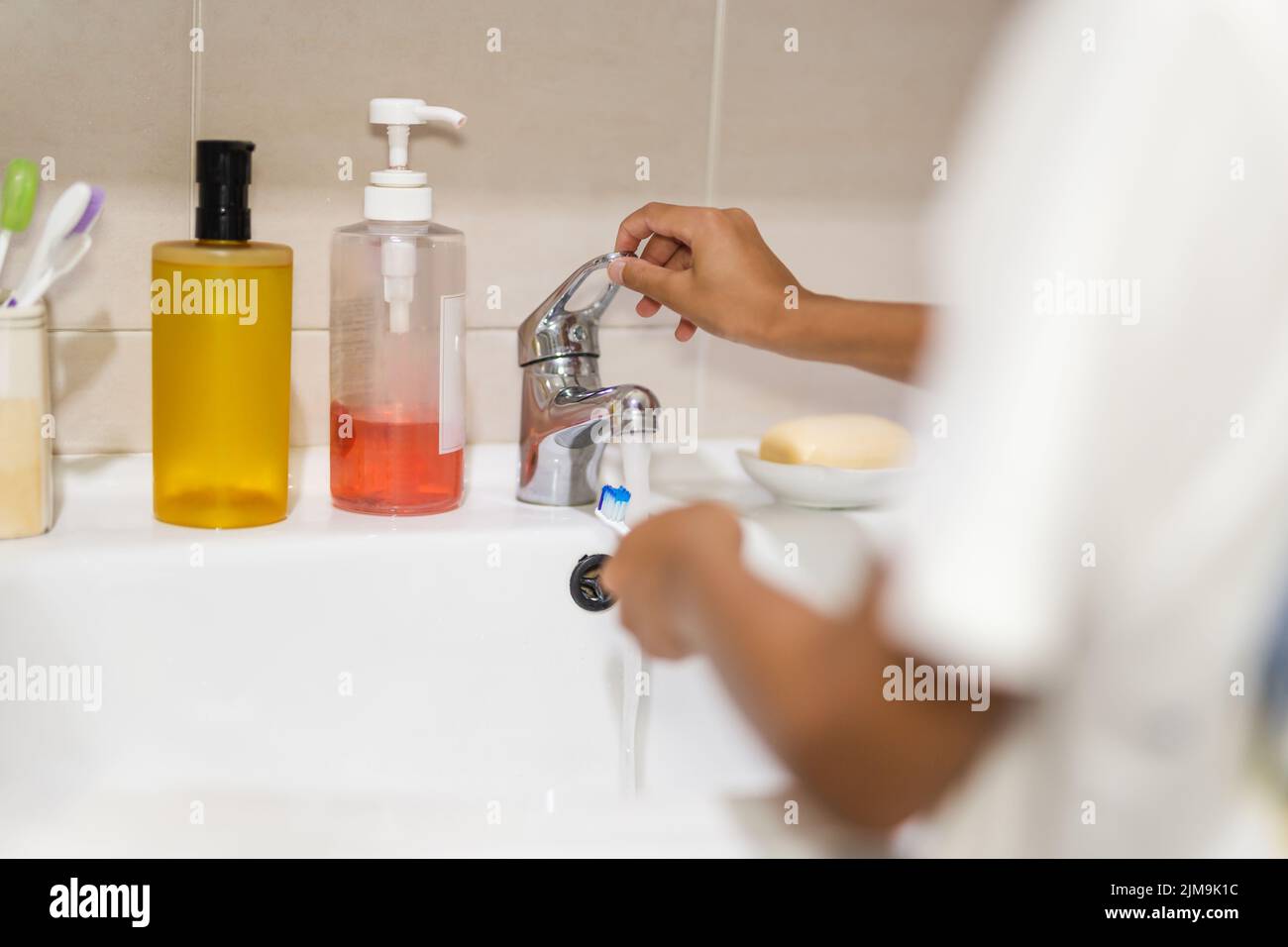 Boy rinsing toothbrush under running tap water in bathroom sink Stock ...