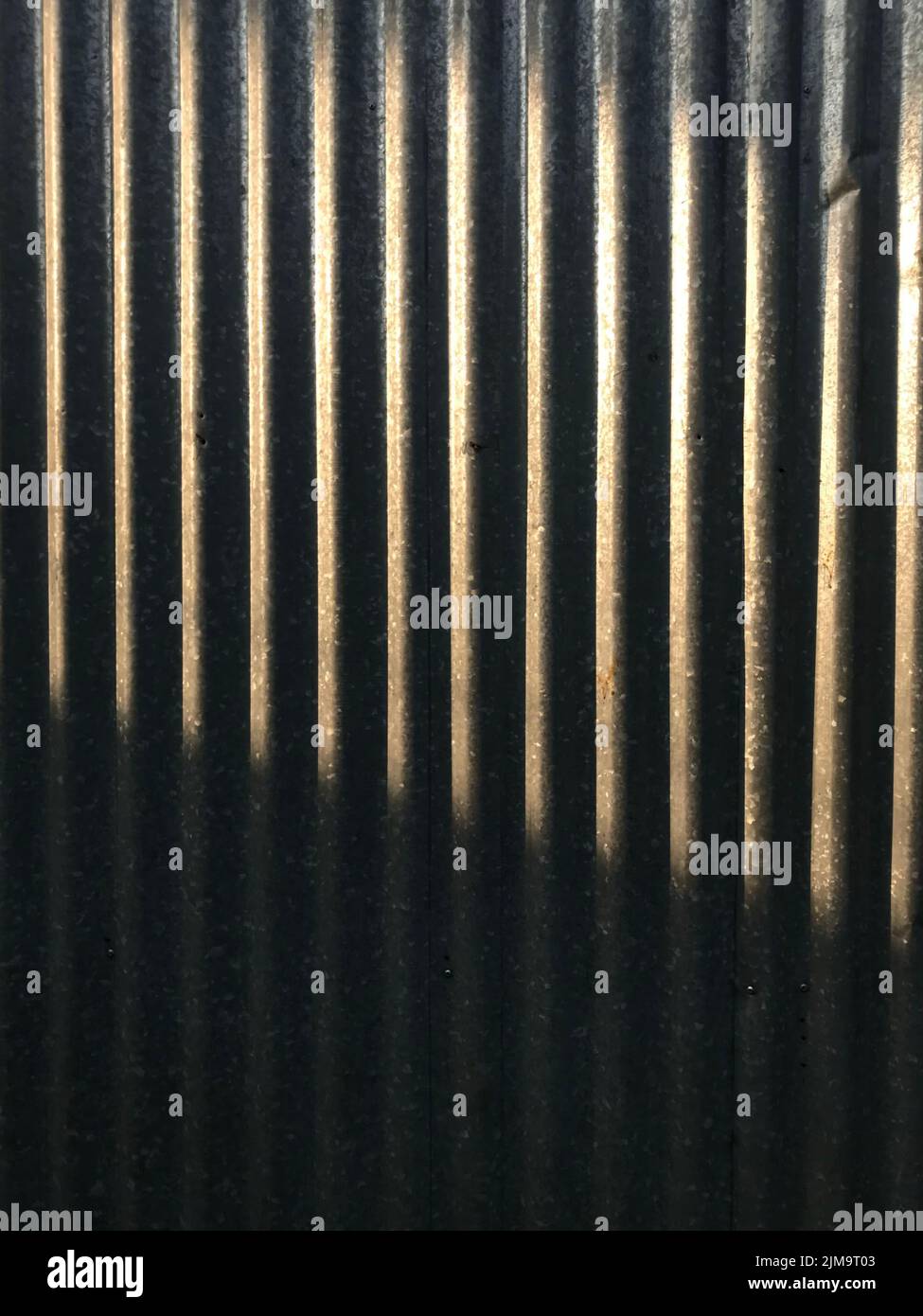 A vertical shot of the sun dropping shadow on a metallic slate fence ...