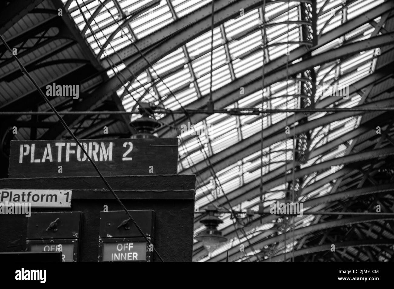 A closeup of a railway station with a steel curved roof overhead and a ...