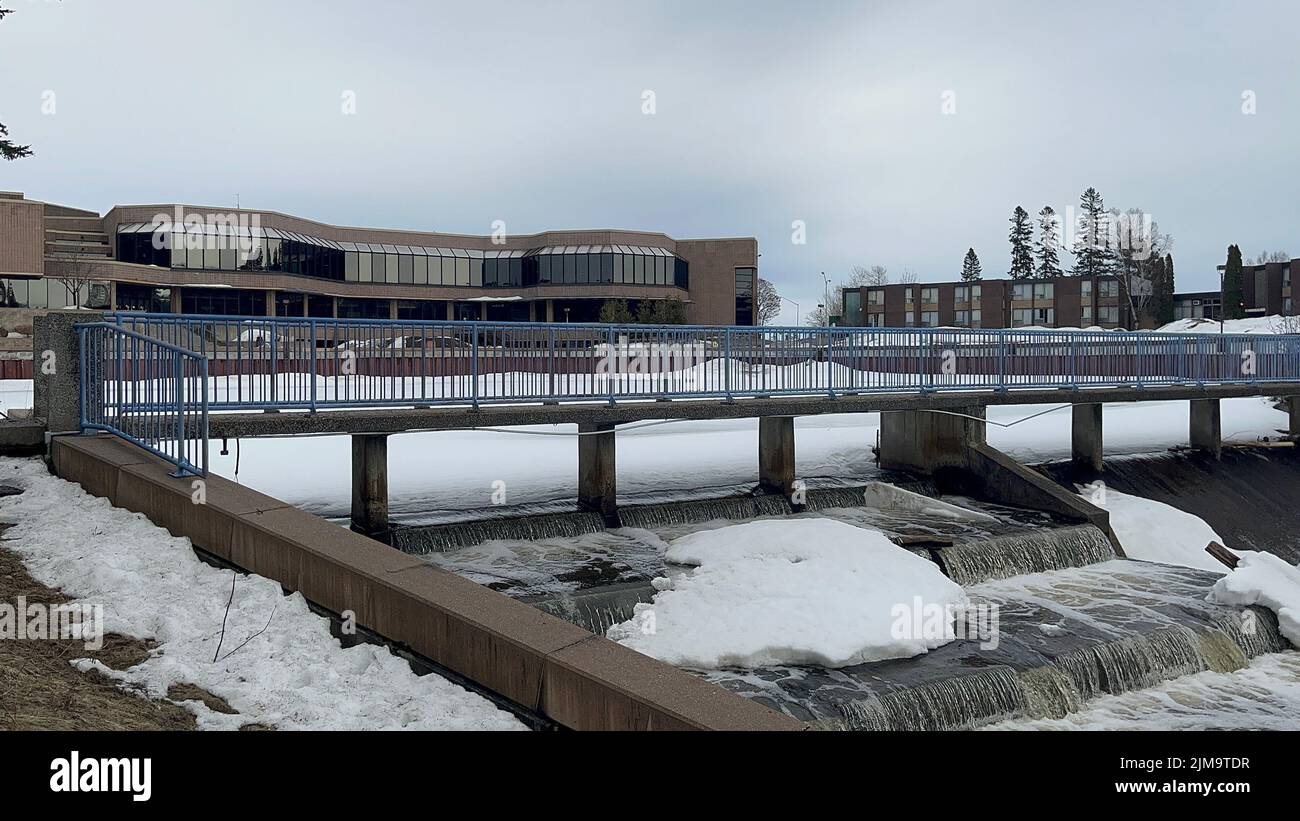 The footbridge over snowy dam water in front of a big building Stock ...