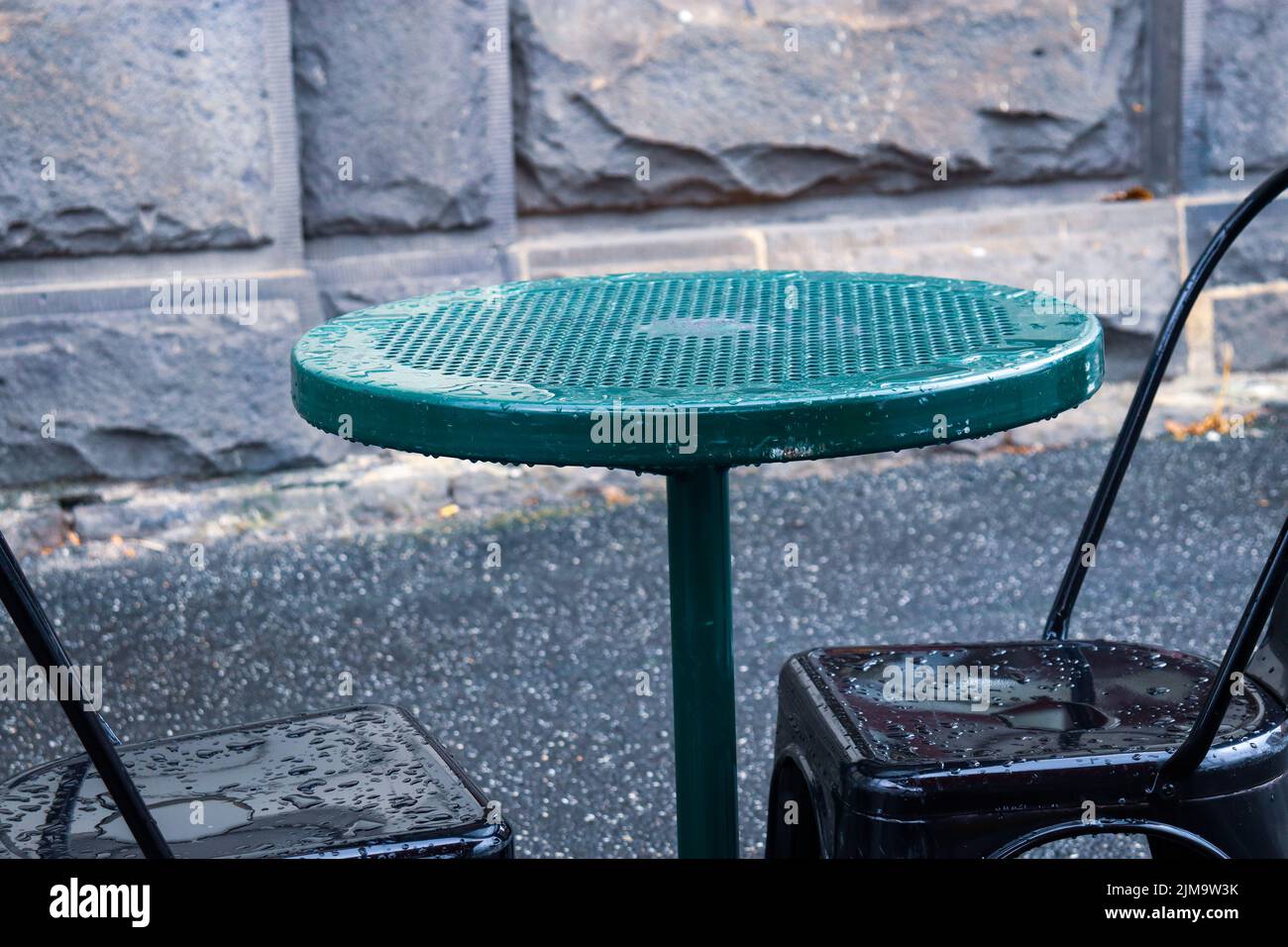 outdoor cafe table and chairs with raindrops and backdrop of stone wall ...