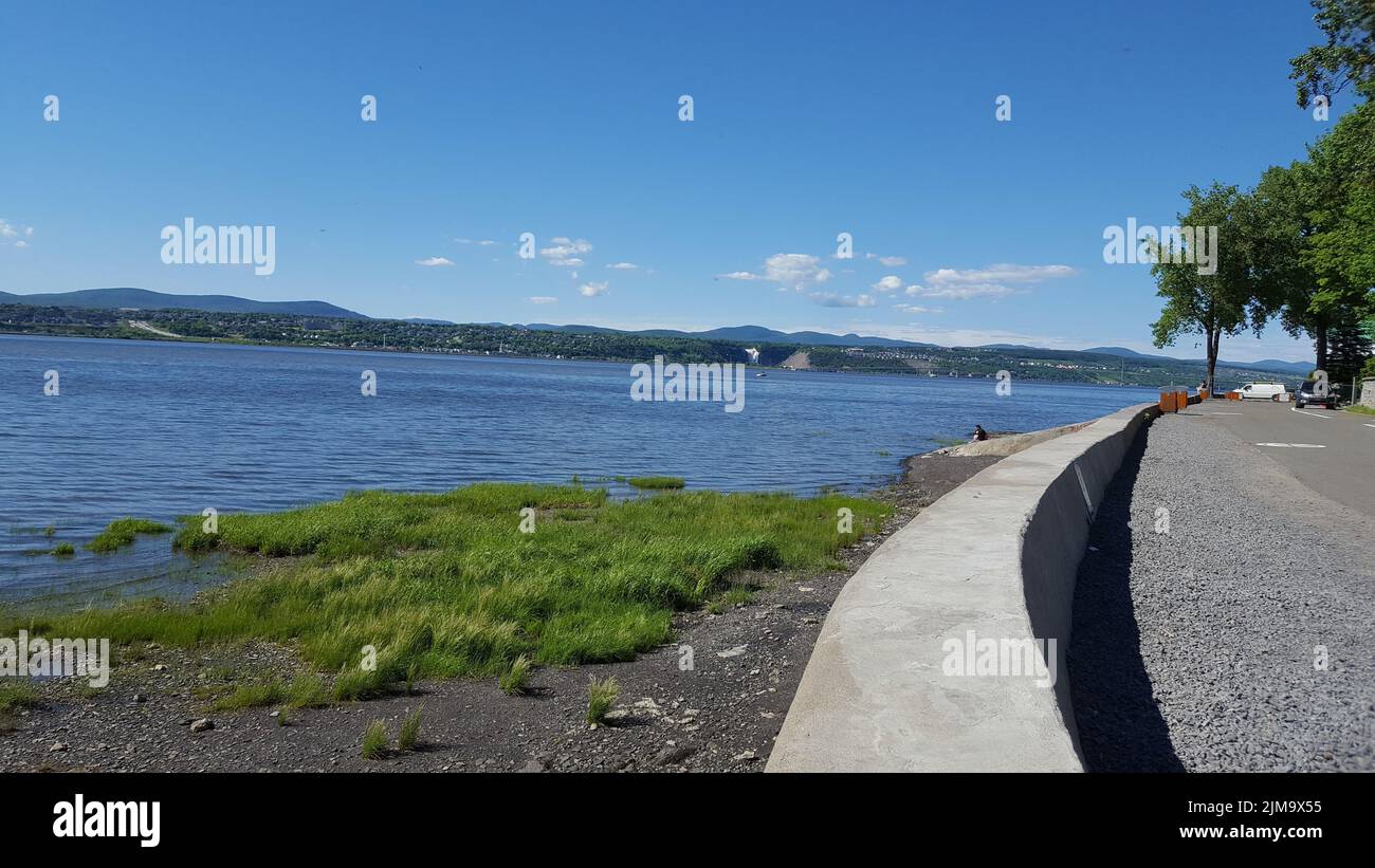 A scenic view of a pavement near a sandy shore covered with green grass ...