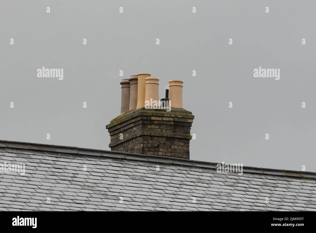 Brick stack with different types of chimney pots together on wet roof against grey sky Stock ...