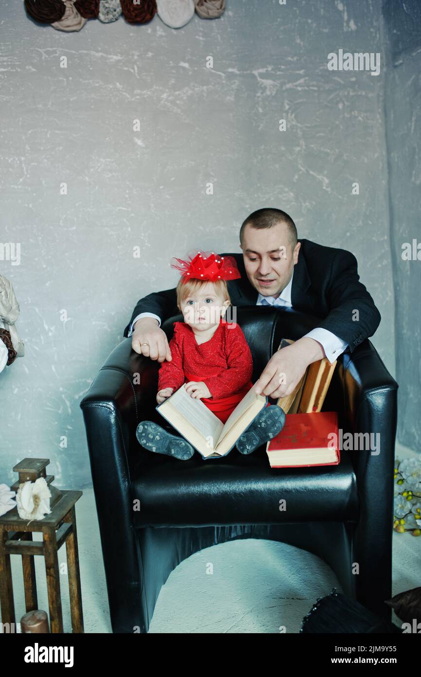 Little cute princess girl with her dad sitting on a chair and read old ...