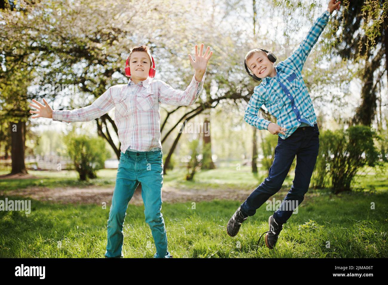Two brother boy with headphones having fun and jump in air on park ...