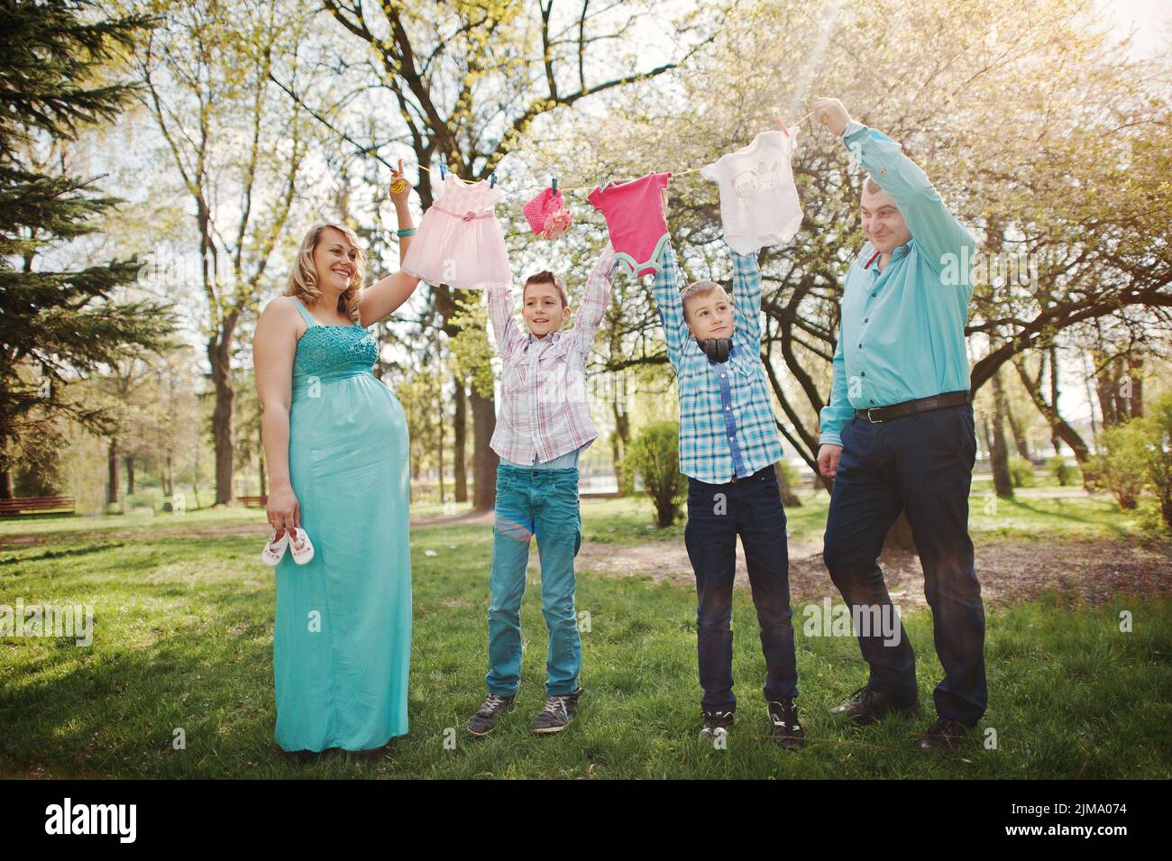 Happy pregnant couple with two sons holding girls' baby clothes on ...