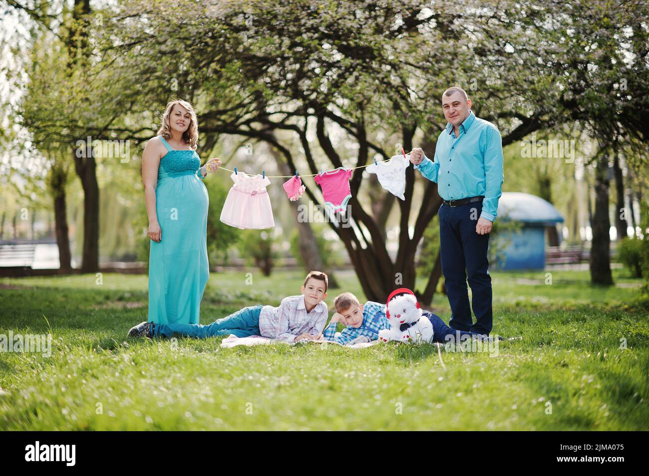 Happy pregnant couple with two sons holding girls' baby clothes on ...