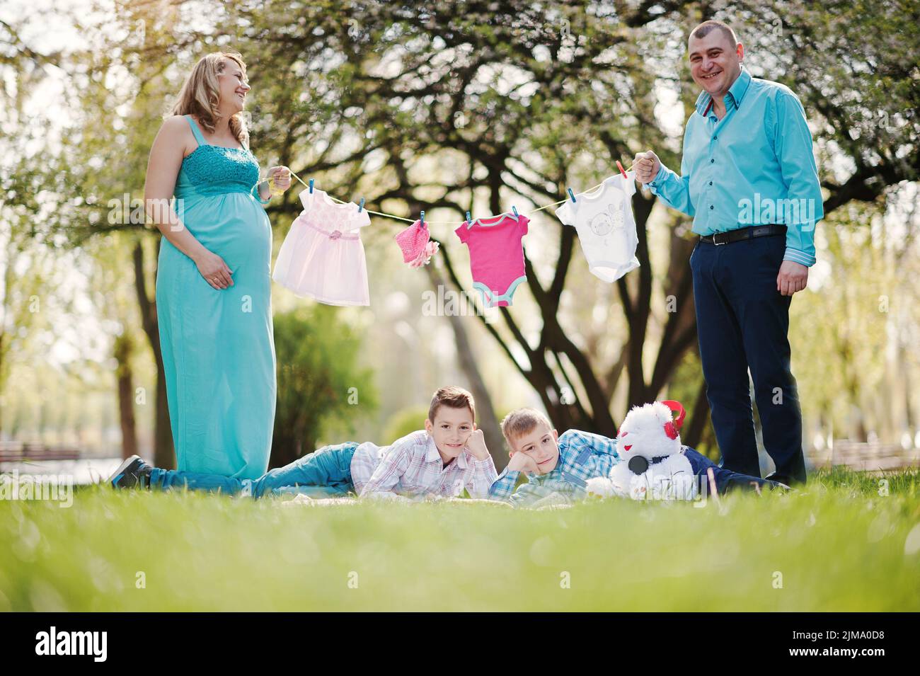 Happy pregnant couple with two sons holding girls' baby clothes on ...