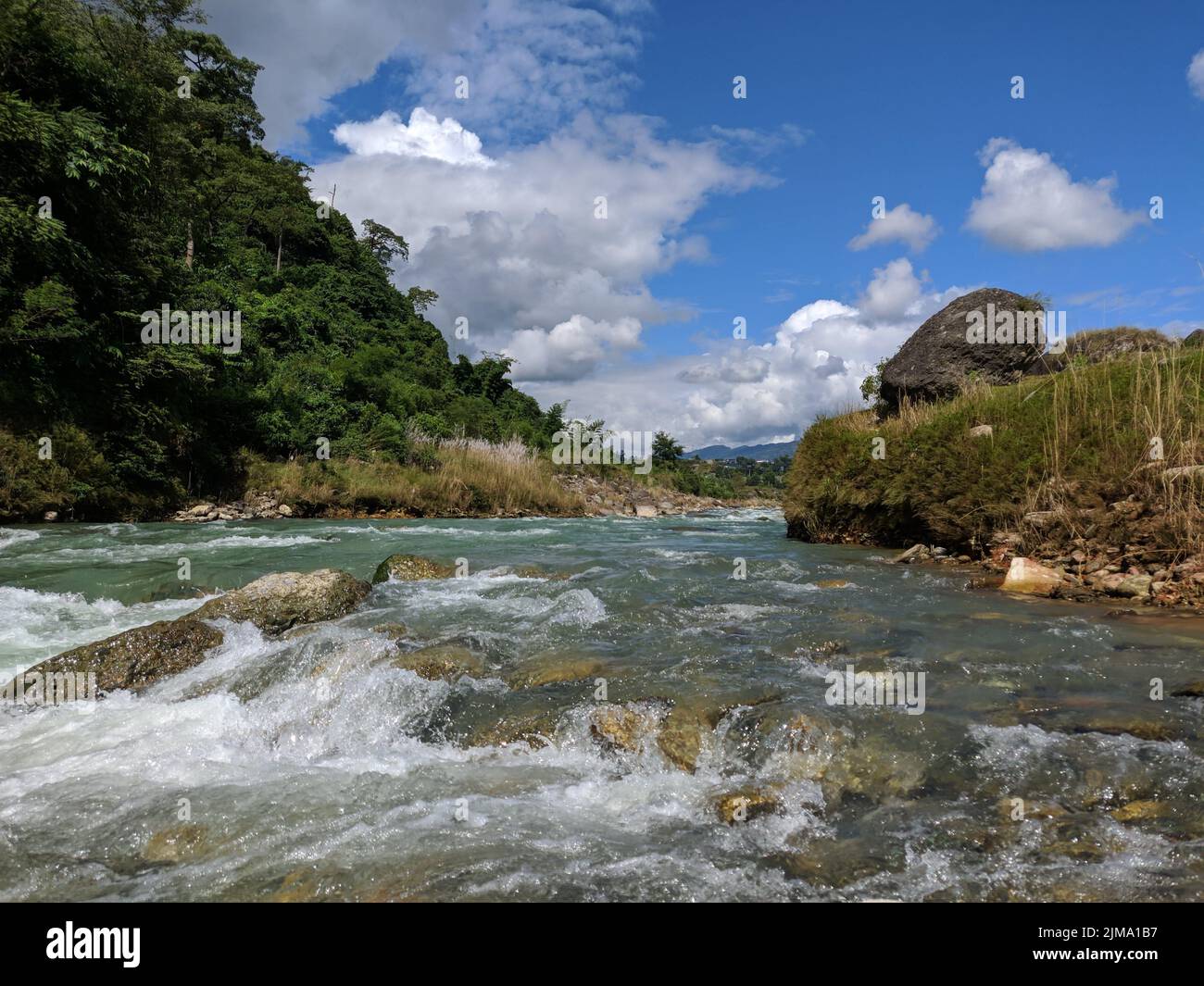 A blue wide shallow river between hills covered with trees on a bright ...