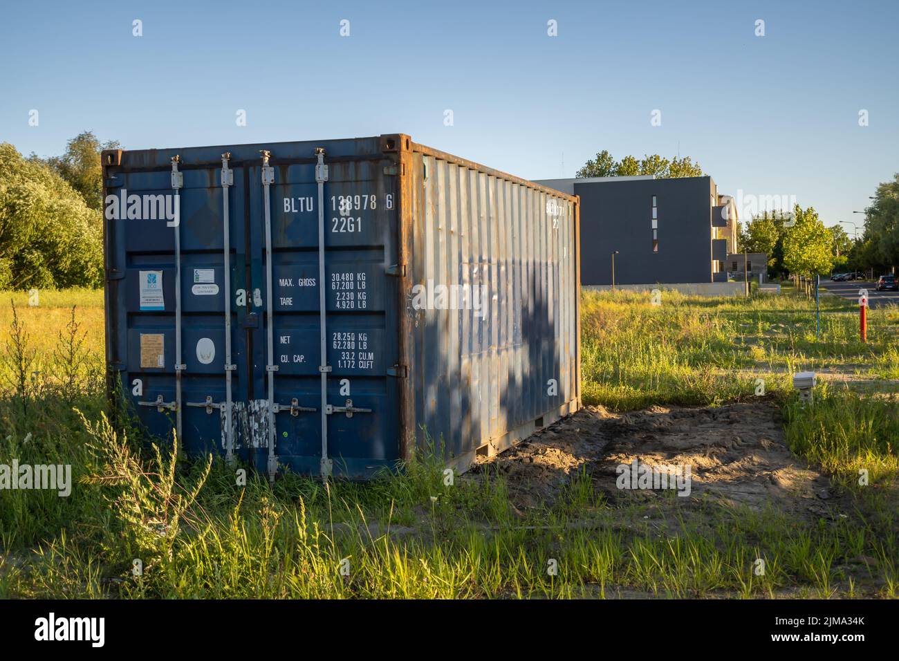 A blue metal container on green weeds near a modern apartment building ...