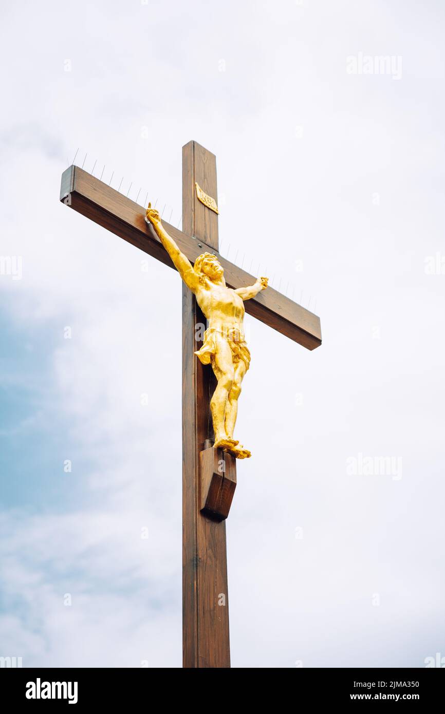 A vertical shot of the golden statue of Jesus Christ on a wooden cross in cloudy sky background ...