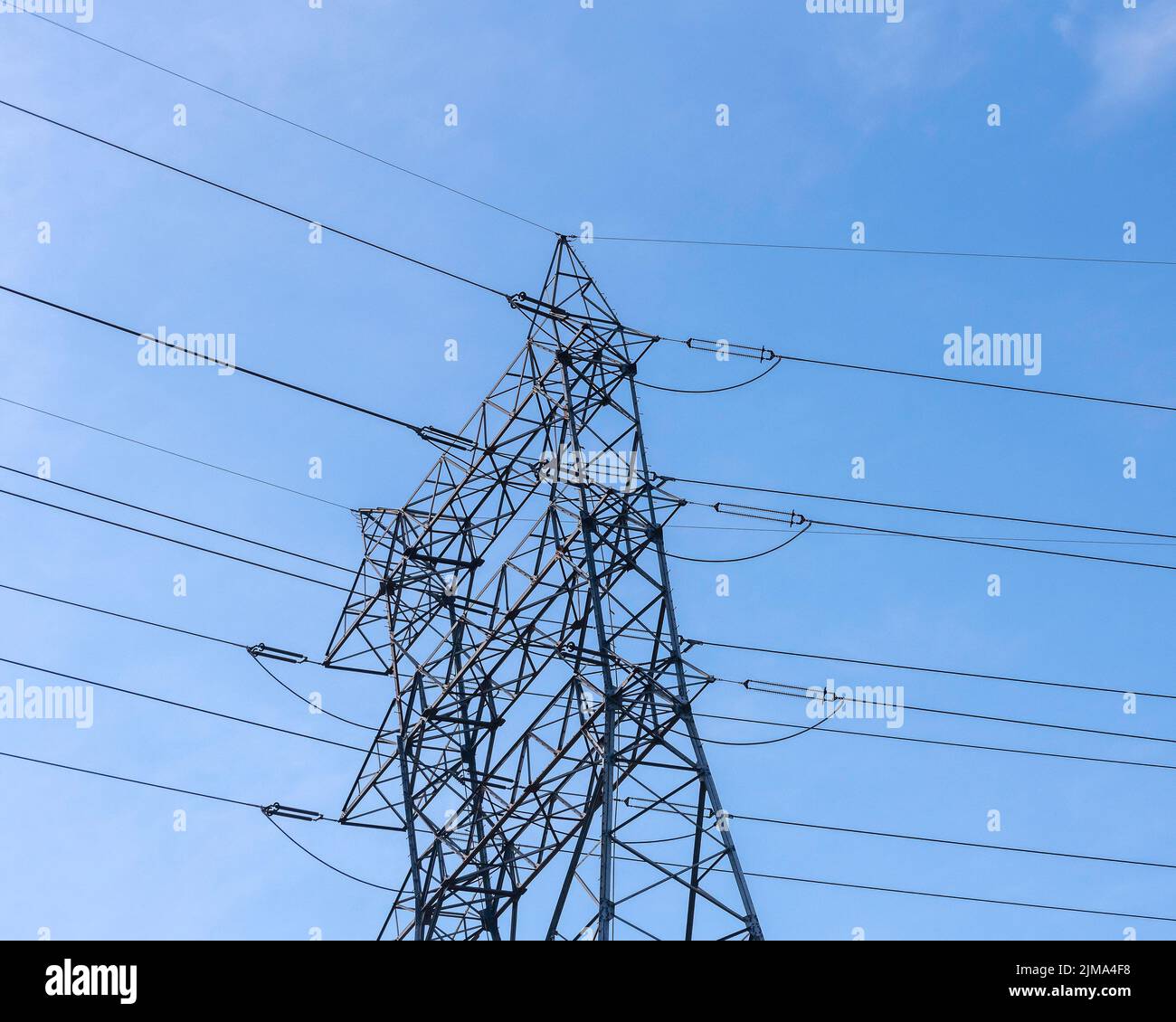 A steel lattice transmission tower stands against a clear blue sky ...